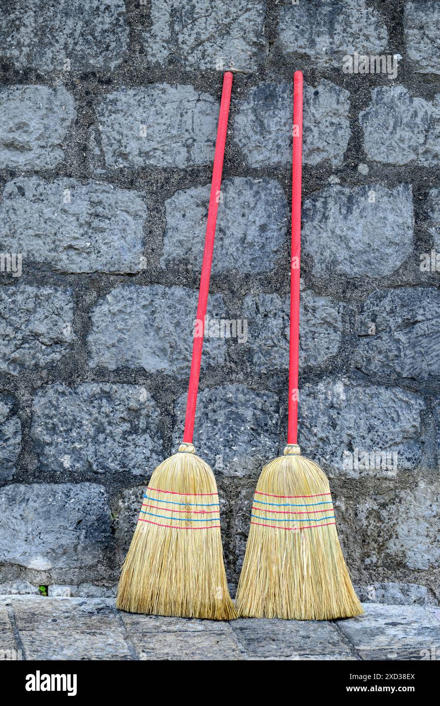 Two brooms with red handles leaning against a stone wall Stock Photo ...