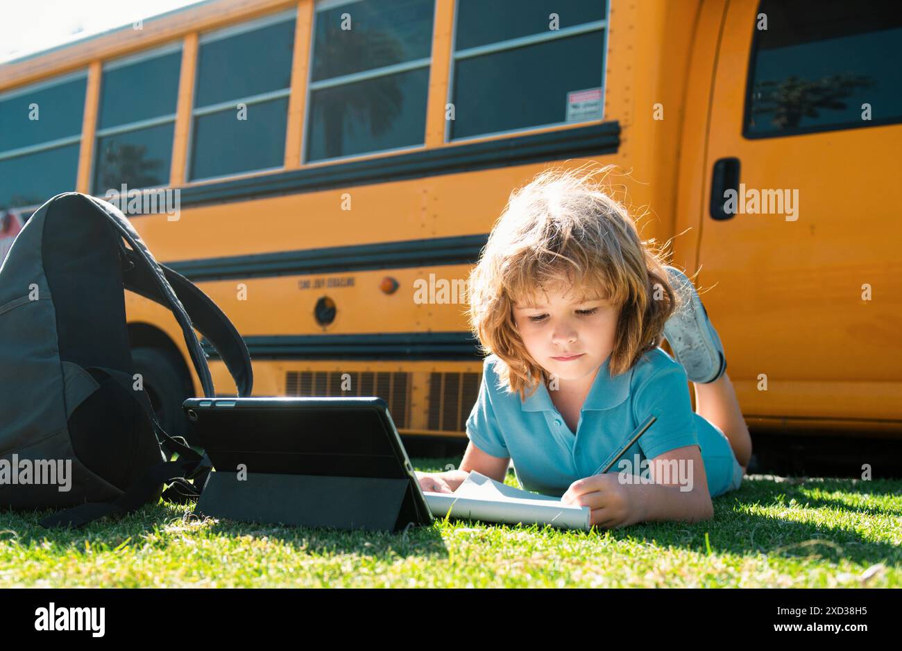 Smart schoolboy on laying on grass with digital tablet at school park ...