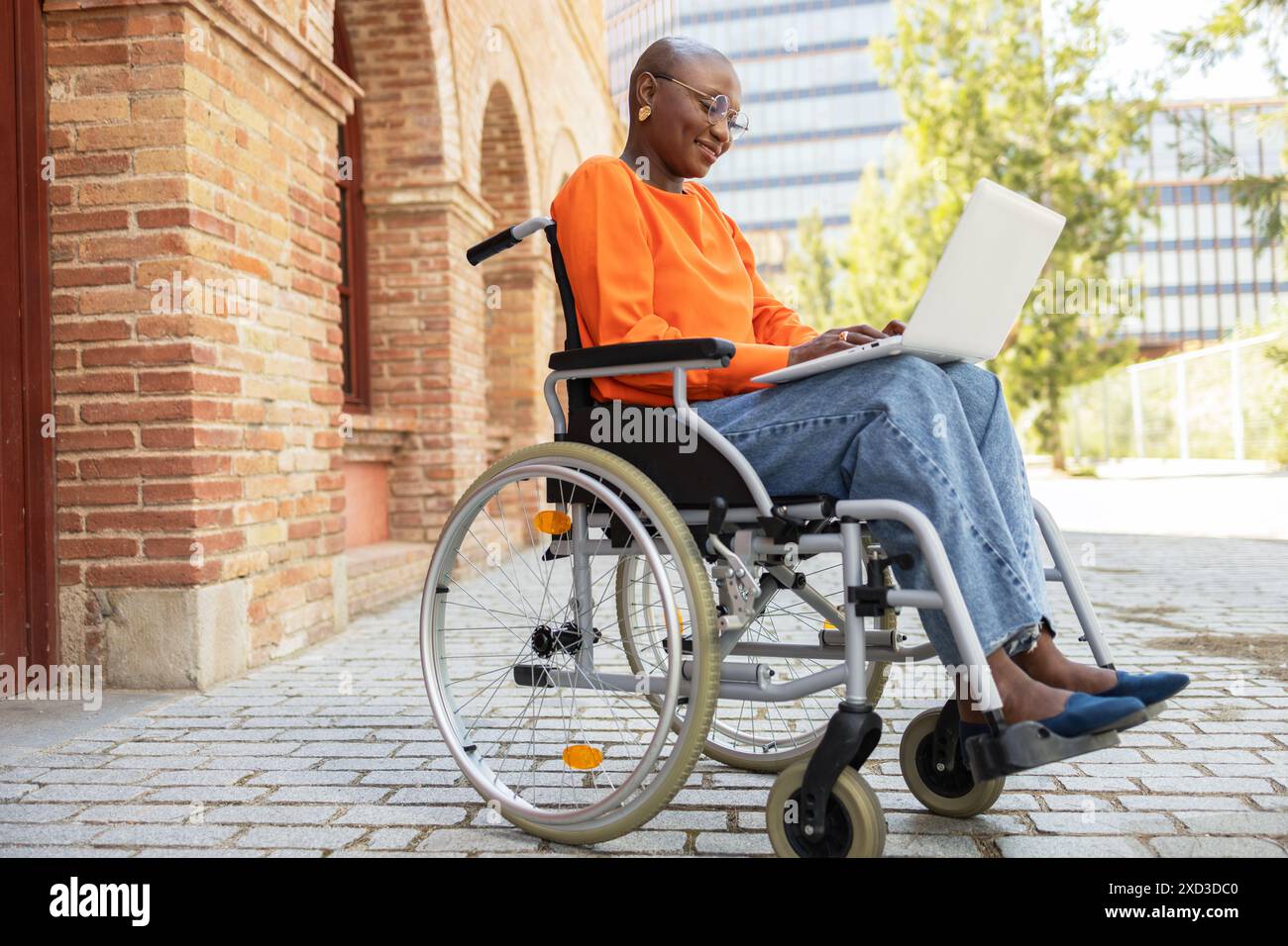 An African American woman in a wheelchair uses a laptop outdoors ...