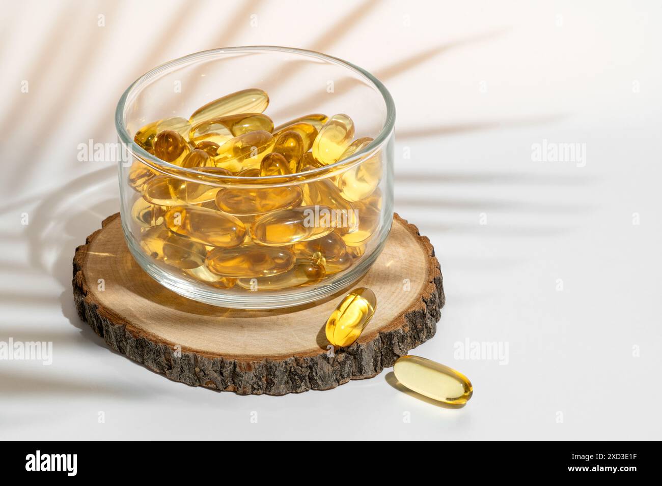 A clear glass bowl filled with golden Omega 3 capsules is placed on a ...