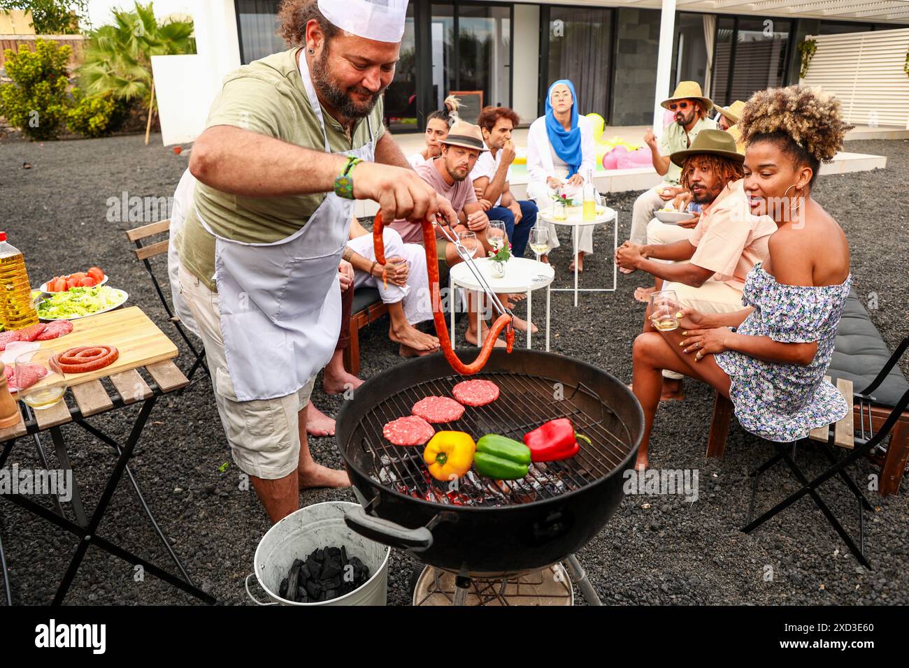 Diverse group of friends gathered around a barbecue as a Caucasian man ...