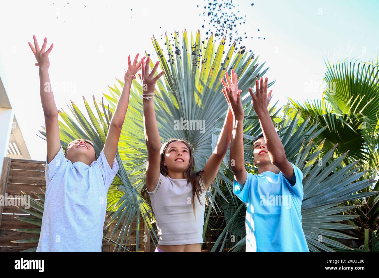 Three children, two boys and a girl, joyously stretch their arms up to ...