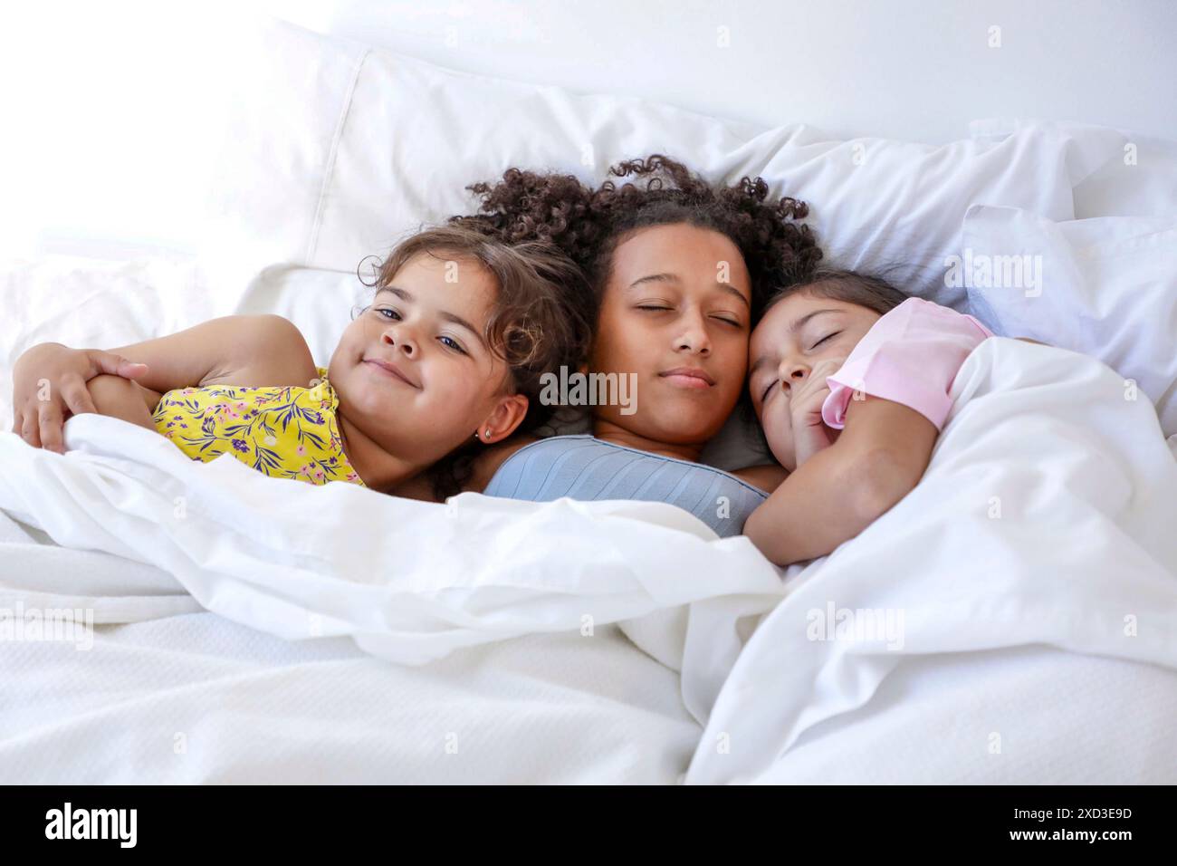 A multiethnic family of three siblings wakes up cozily nestled together ...