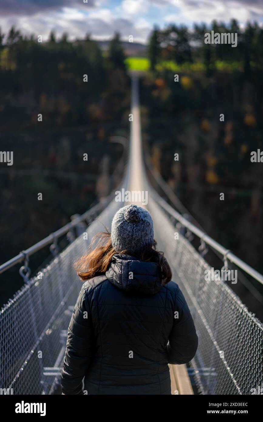 Back view of unrecognizable woman walks across the Geierlay suspension ...
