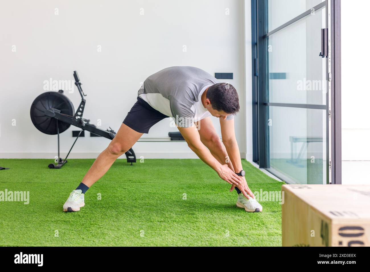 A young man performs a stretching exercise on the vibrant green ...