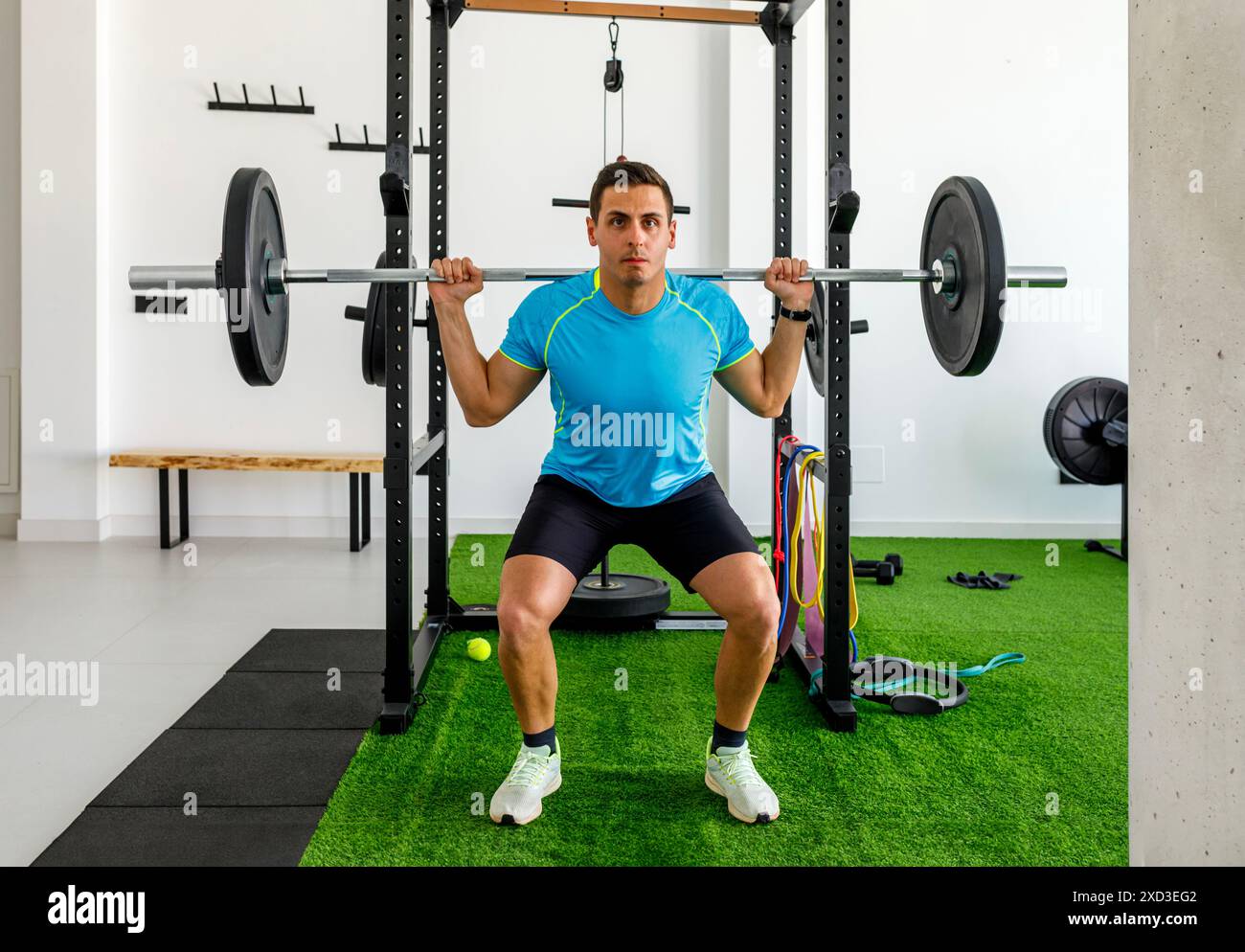 A focused man performs a barbell squat in a well-equipped, contemporary ...