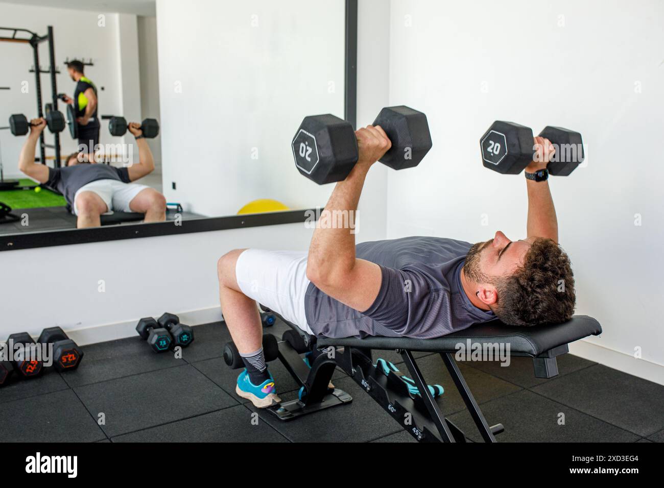 A focused man works out, performing a dumbbell bench press in a well ...