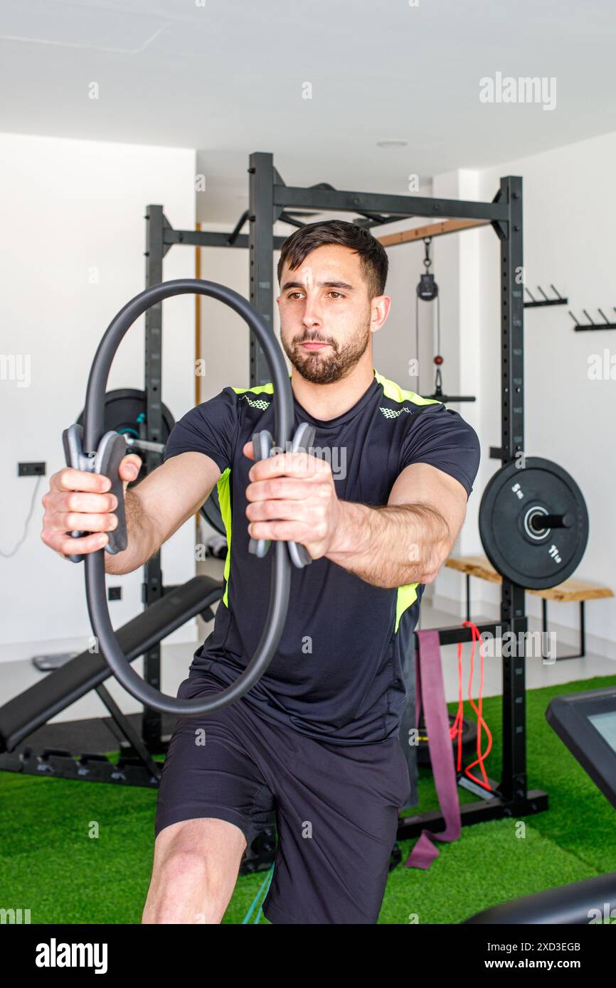 A focused young man in a black and green gym vest utilizes resistance ...
