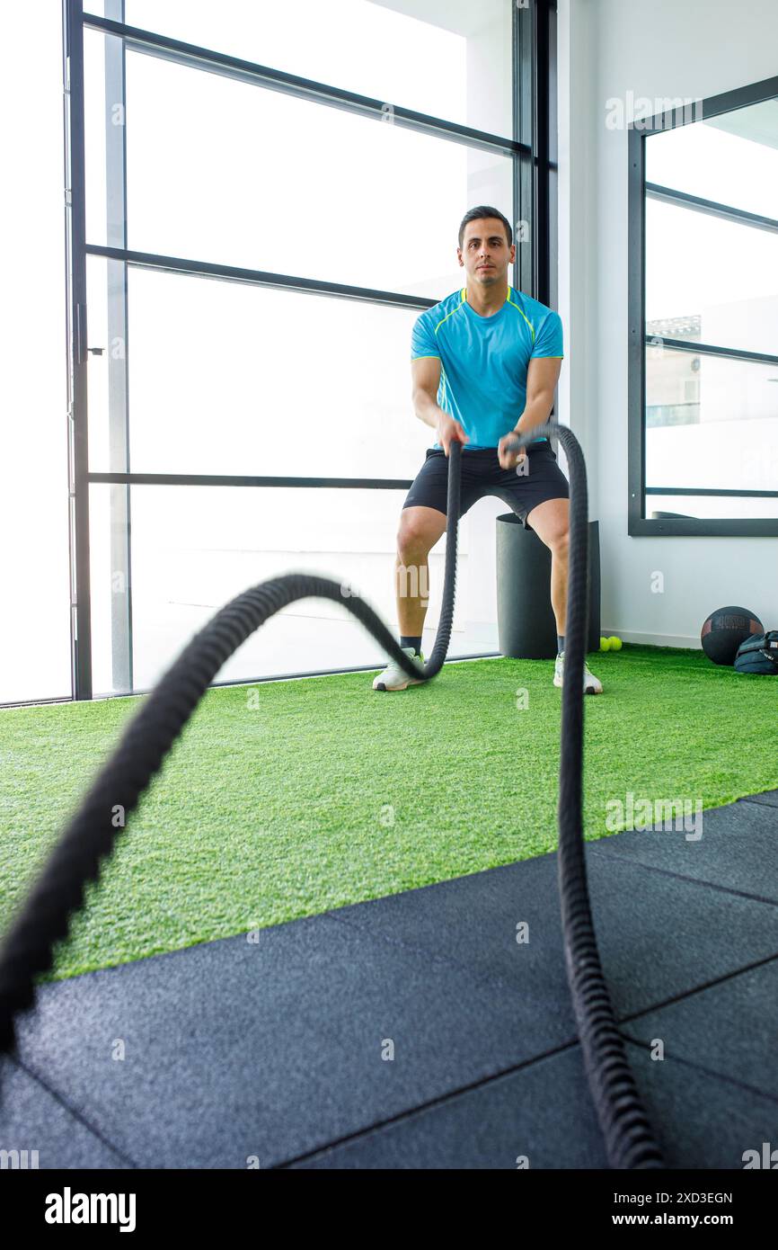 An athletic man performs an intense battle rope workout at a gym with a ...