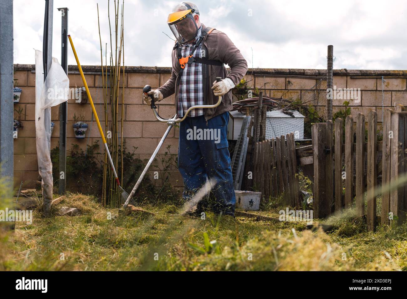 A man in safety gear trims tall, wild grass in a cluttered backyard ...