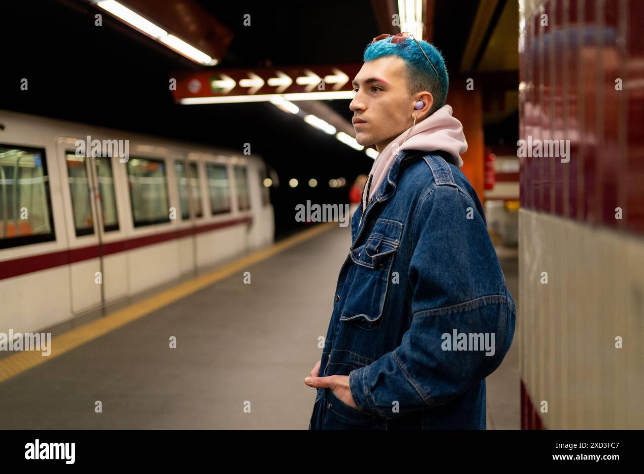 A young man with vibrant blue hair and casual denim attire waits ...