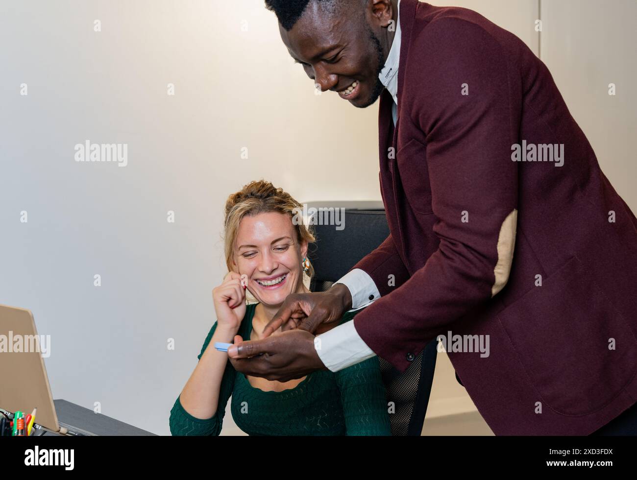 Two joyful coworkers sharing a laugh over a smartphone at their desk in ...