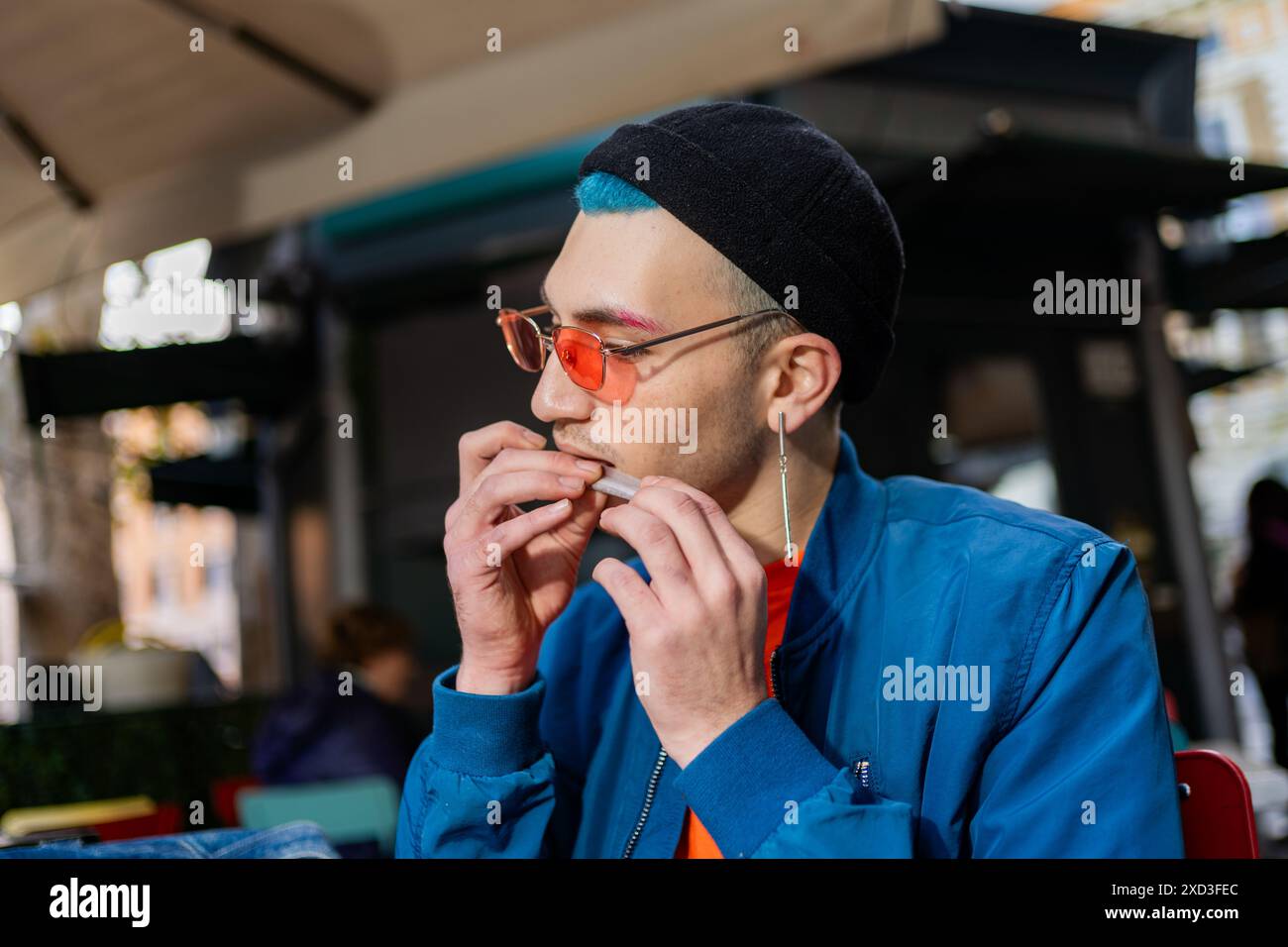 A stylish young man enjoys a hamburger at a street cafe He’s dressed in ...