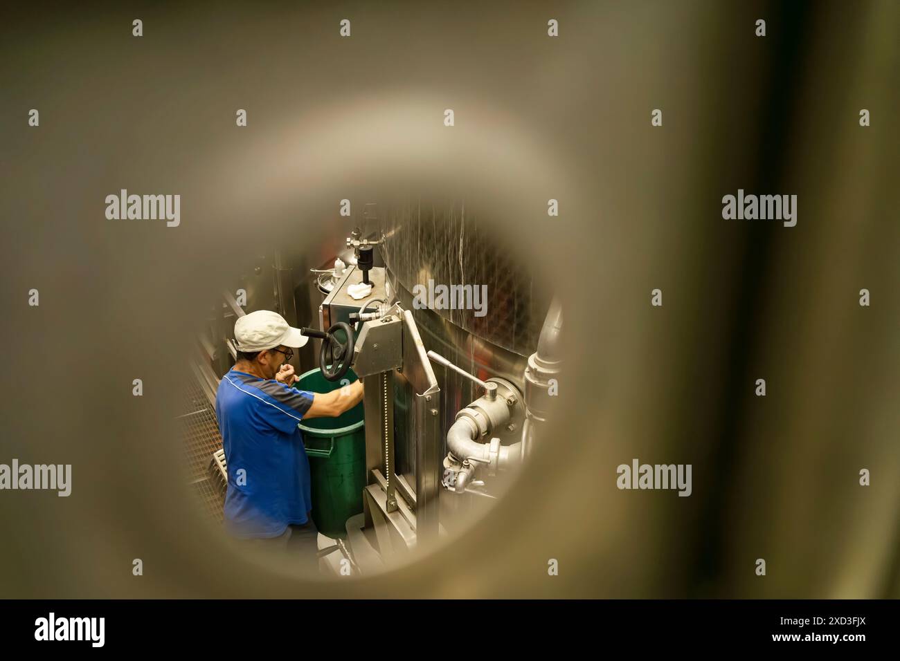 A winery worker is seen through a circular opening, expertly operating ...