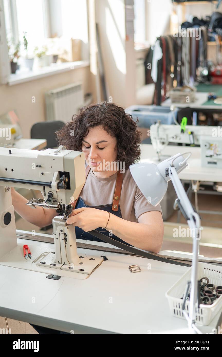 A woman tanner sews a leather belt on a sewing machine. Vertical photo ...