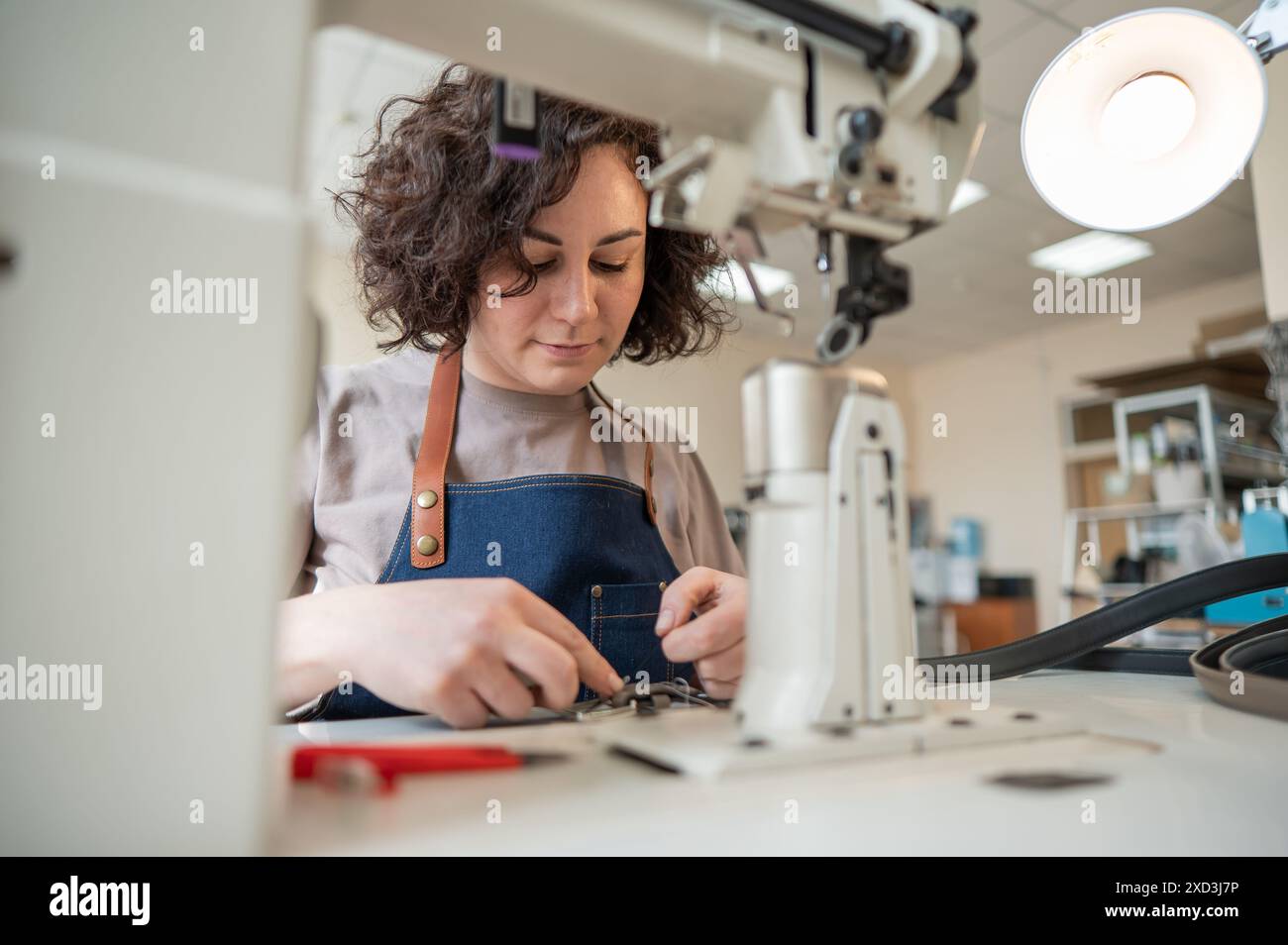 A woman tanner sews a leather belt on a sewing machine Stock Photo - Alamy