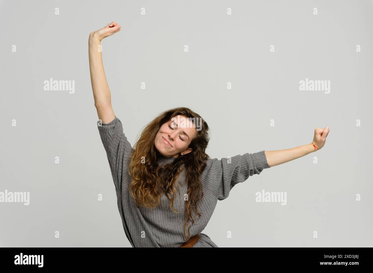 A young attractive woman with long hair stretches, raising her arms above her head. Woman waking ...