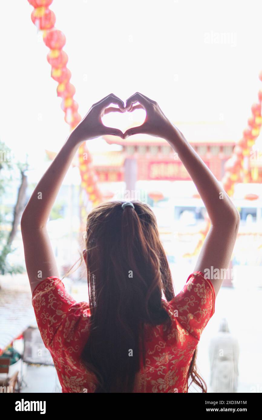 A young woman raises her hands to make a heart symbol meaning love and ...