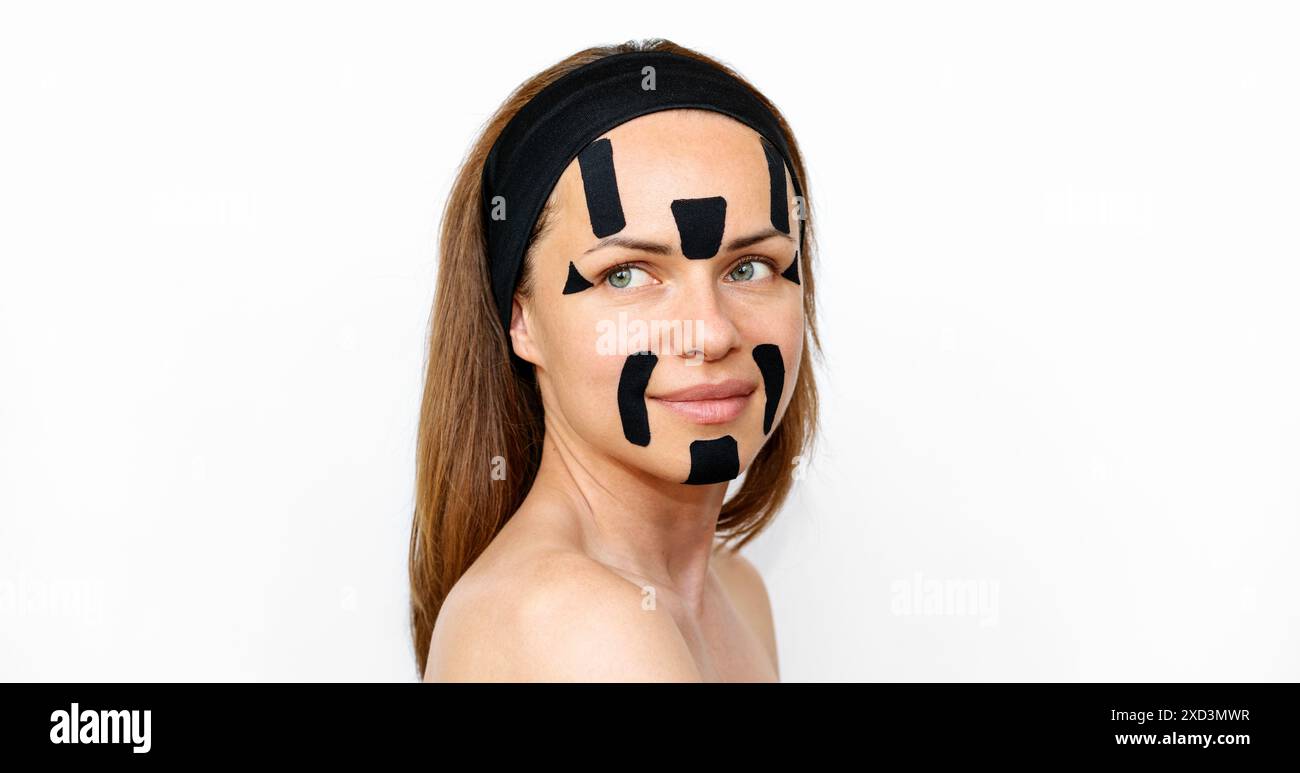 Beautiful caucasian brunette woman applying kinesio tapes to her face ...
