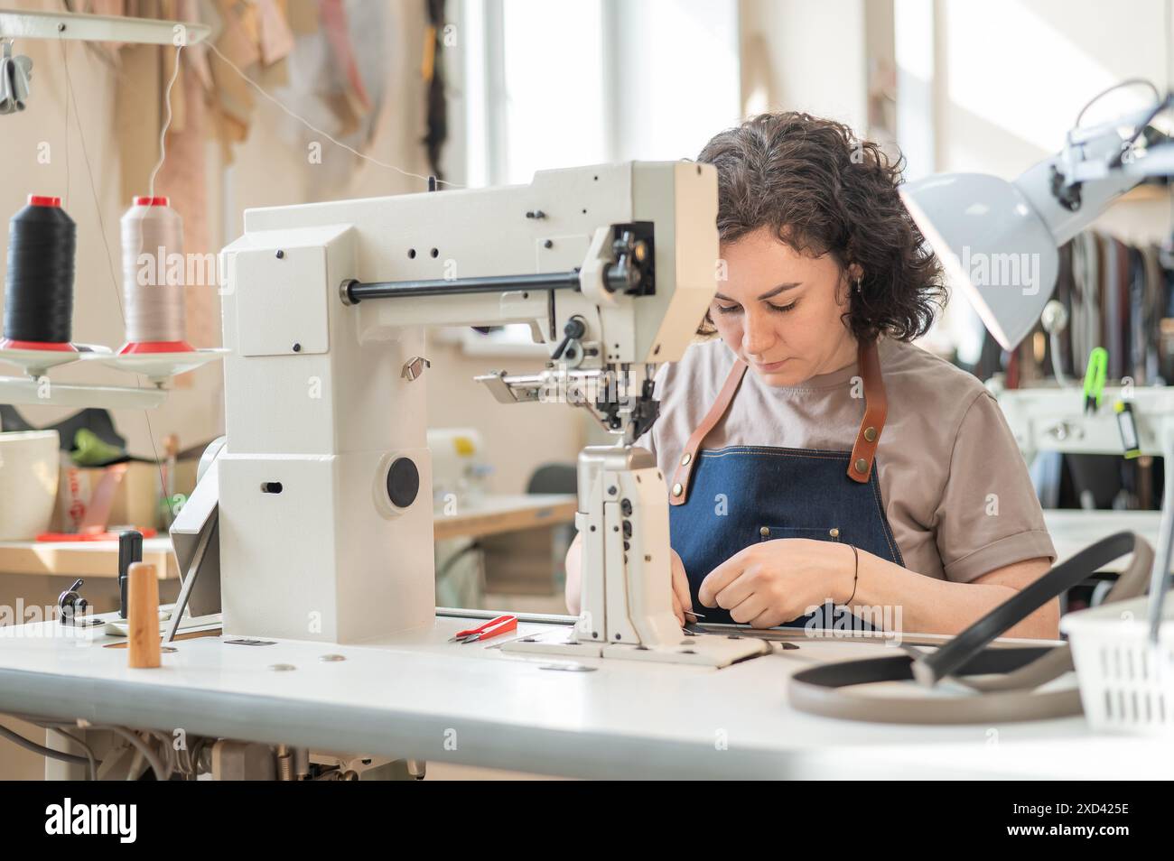 A woman tanner sews a leather belt on a sewing machine Stock Photo - Alamy
