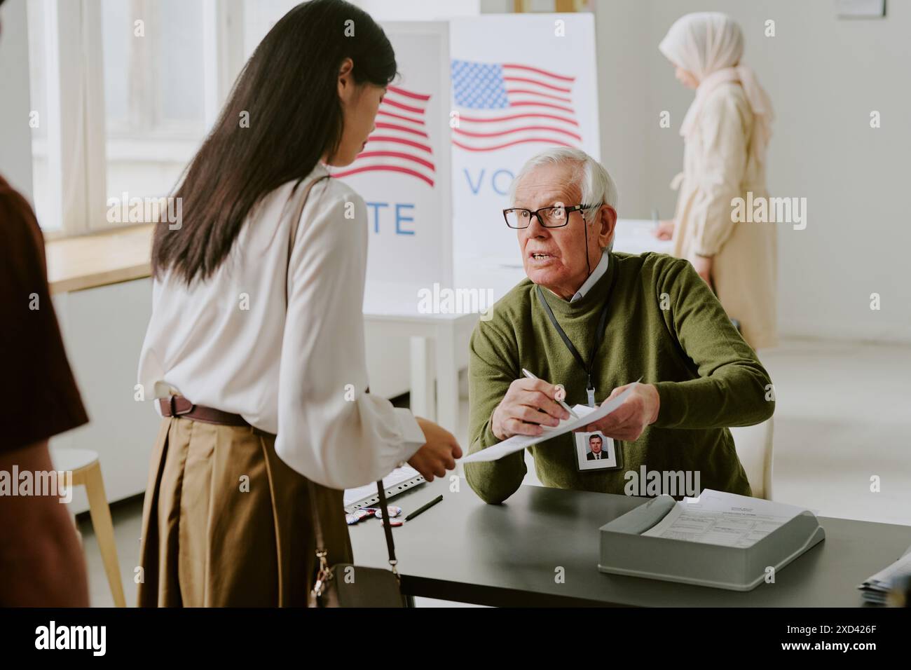 Senior Caucasian electoral district worker sitting at desk at polling ...