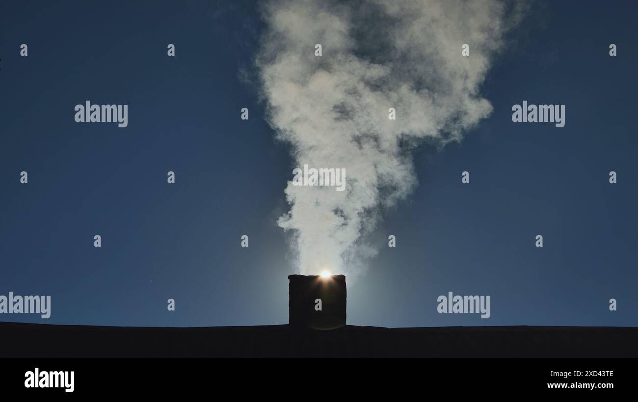 Silhouette of smoke against the sun from the chimney of a village house ...