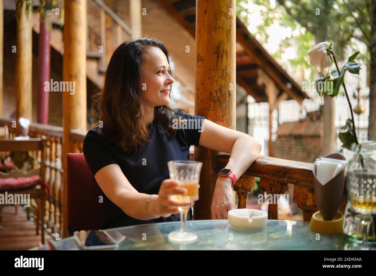 Cheerful and relaxed woman drinking white wine at rustic outdoor cafe enjoying tranquil ambiance ...