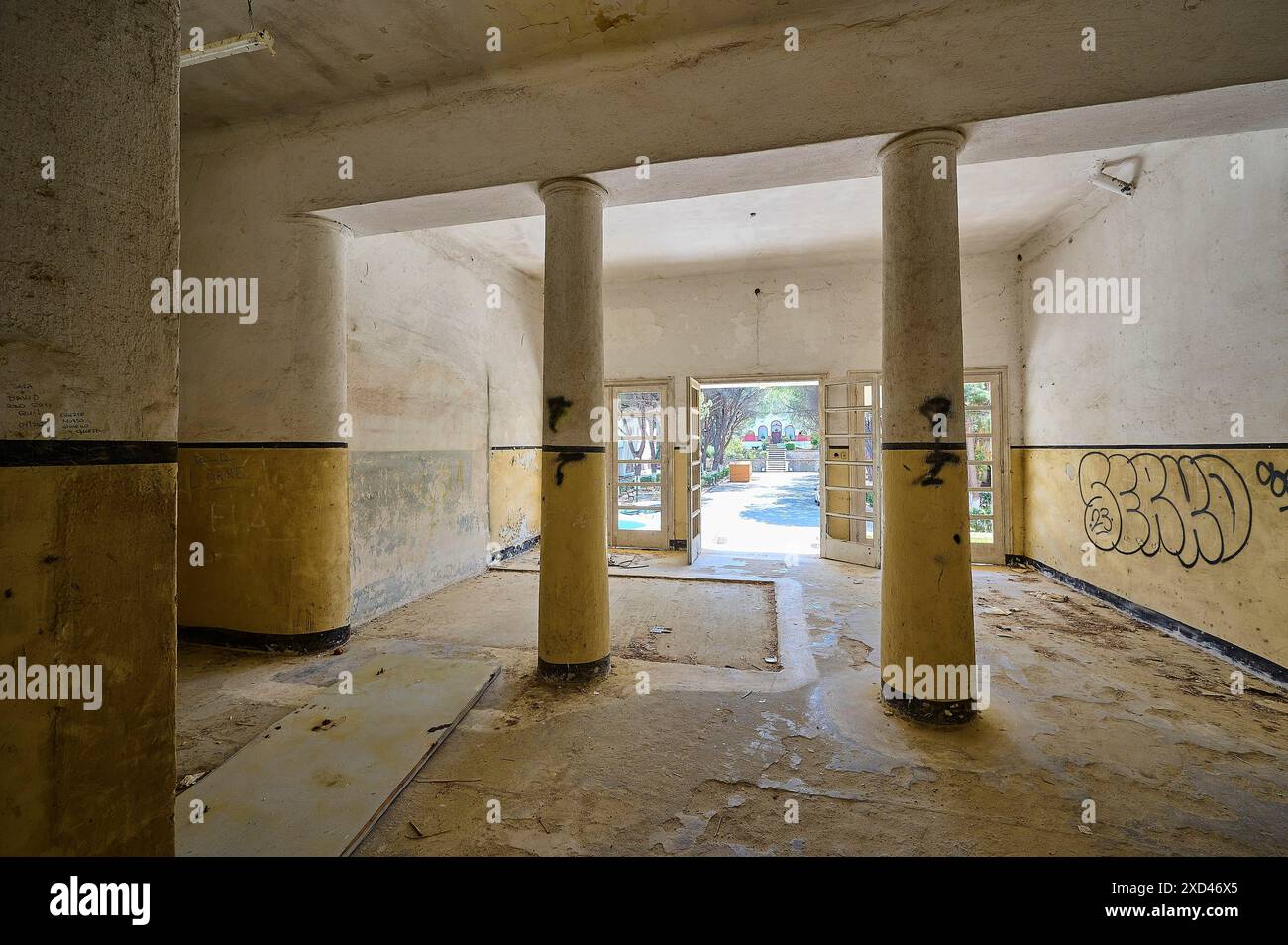 An abandoned corridor with columns, graffiti on the walls and daylight ...