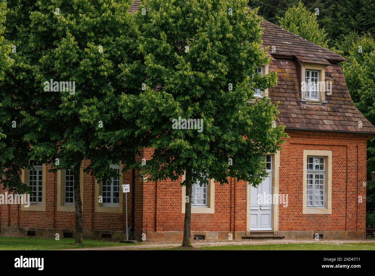 Small historic brick house with white windows and surrounded by green ...