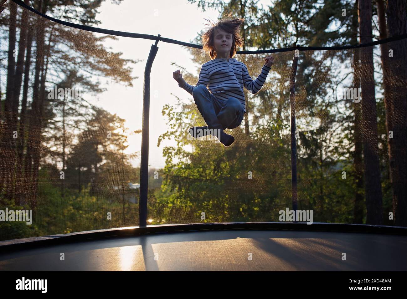 Sweet preteen boy jumping on trampoline making somersaults in the air ...