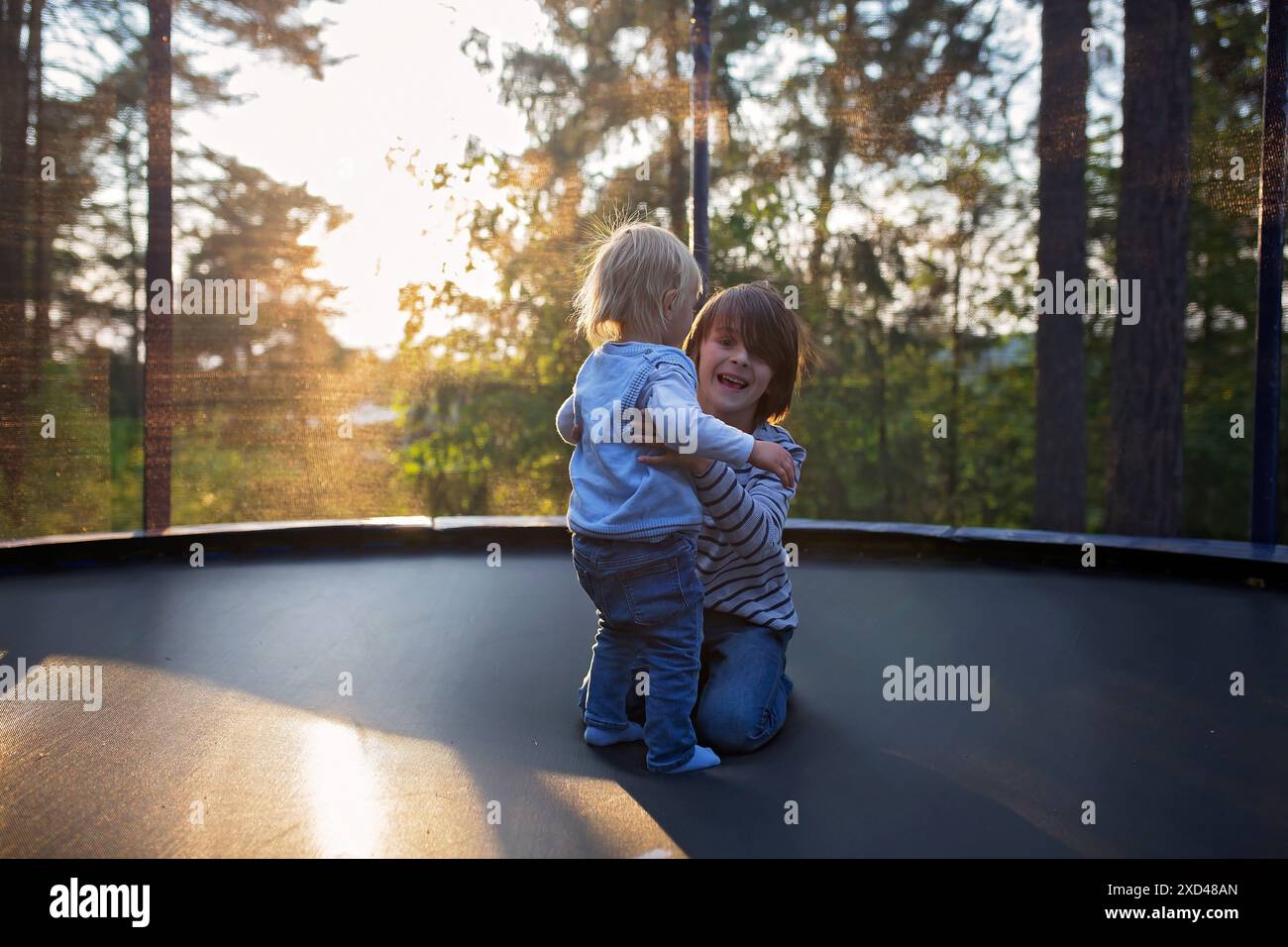 Sweet preteen boy and his toddler brother jumping on trampoline. Happy ...