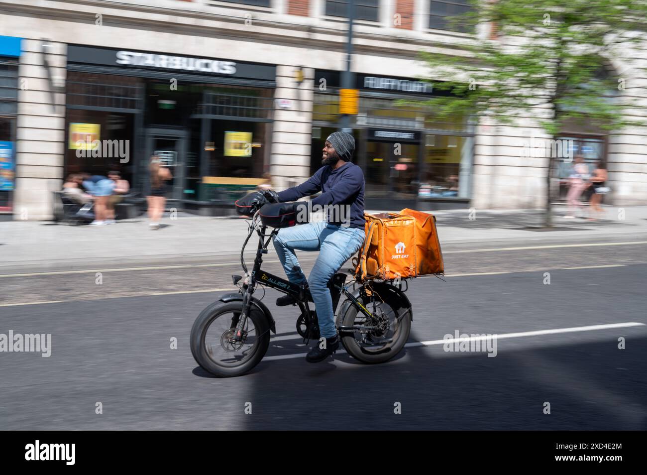 Food delivery cyclist riding an e-bike through the centre of Leeds on a ...