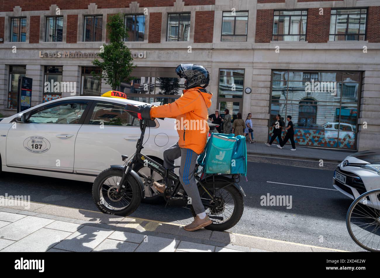 Food delivery cyclist riding an e-bike waiting at traffic lights in the ...
