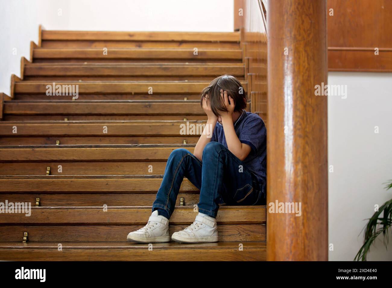 Sad child, sitting on a staircase in a big house, concept for bullying ...