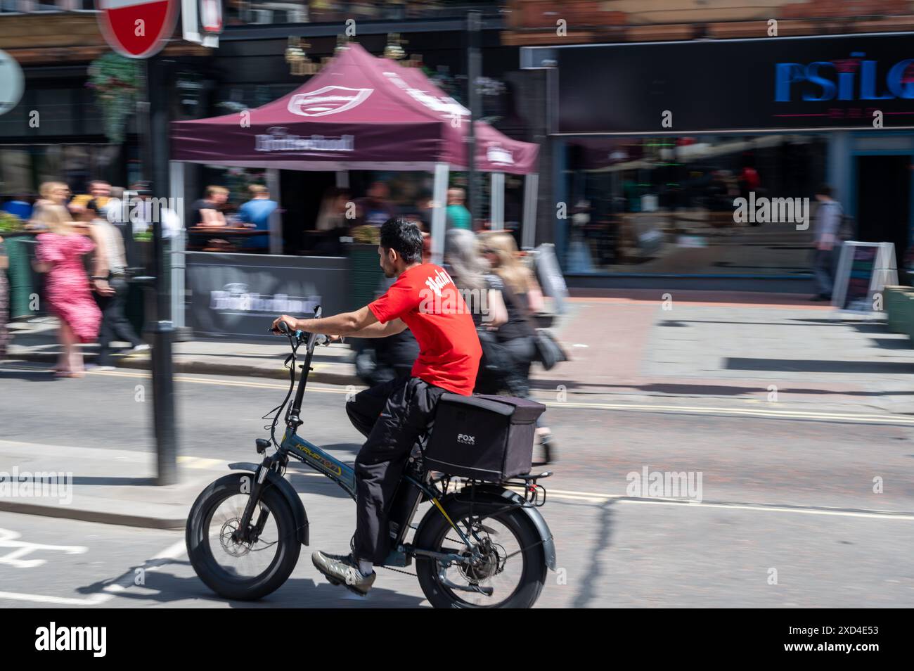 A young Asian male delivery rider rides an e-bike through the centre of ...