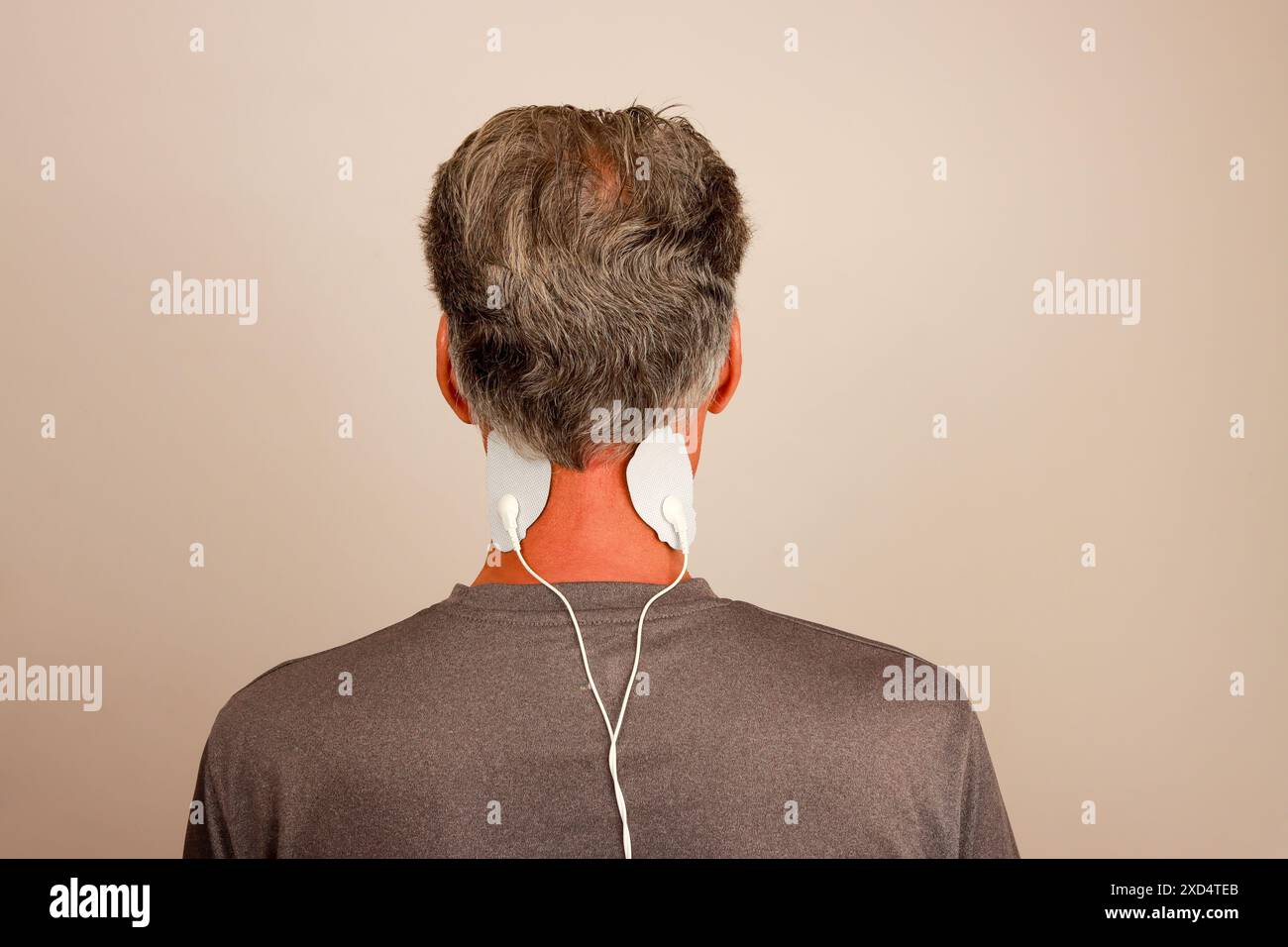 A middle-aged man using a TENS unit for neck pain relief, viewed from ...