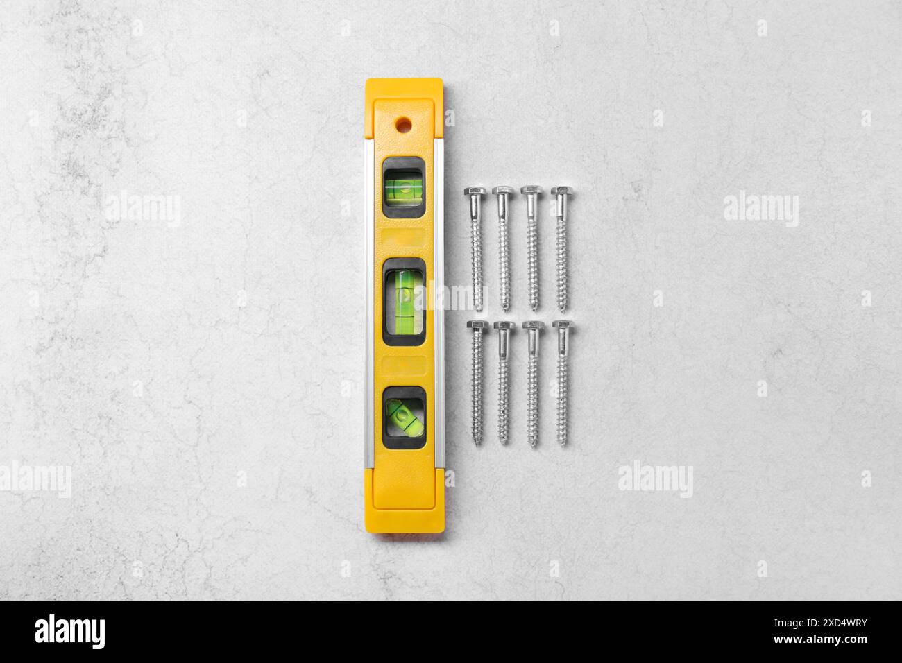 Yellow building level and screws on grey table, flat lay. Construction ...