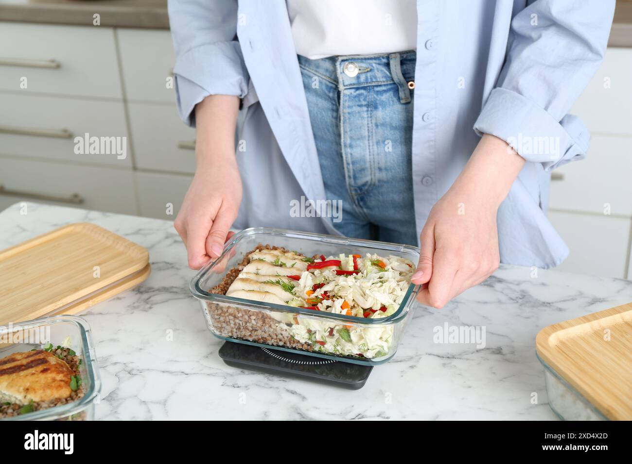 Healthy meal. Woman weighing glass container with food on kitchen scale ...