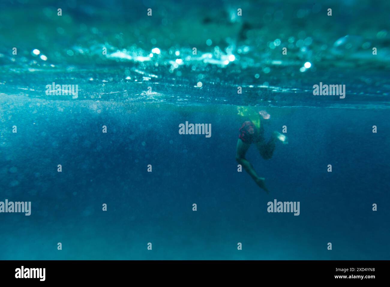 A single swimmer descends beneath the surface of a tropical ocean ...