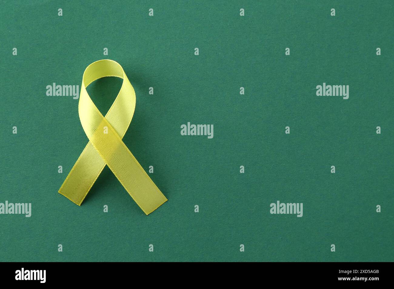 Yellow awareness ribbon on green background, top view. Space for text ...