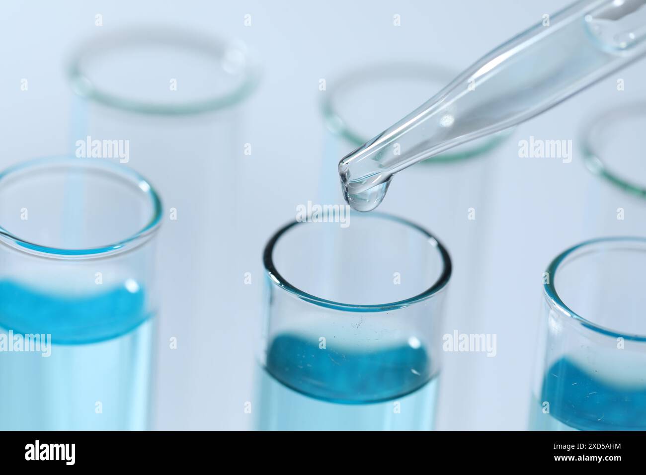 Dripping liquid from pipette into test tube on light background ...