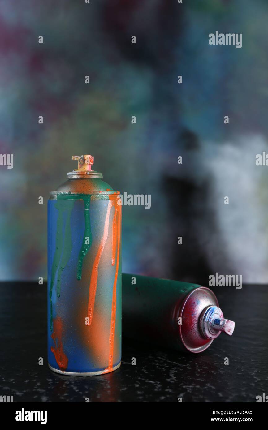Two spray paint cans on black textured surface against color background ...
