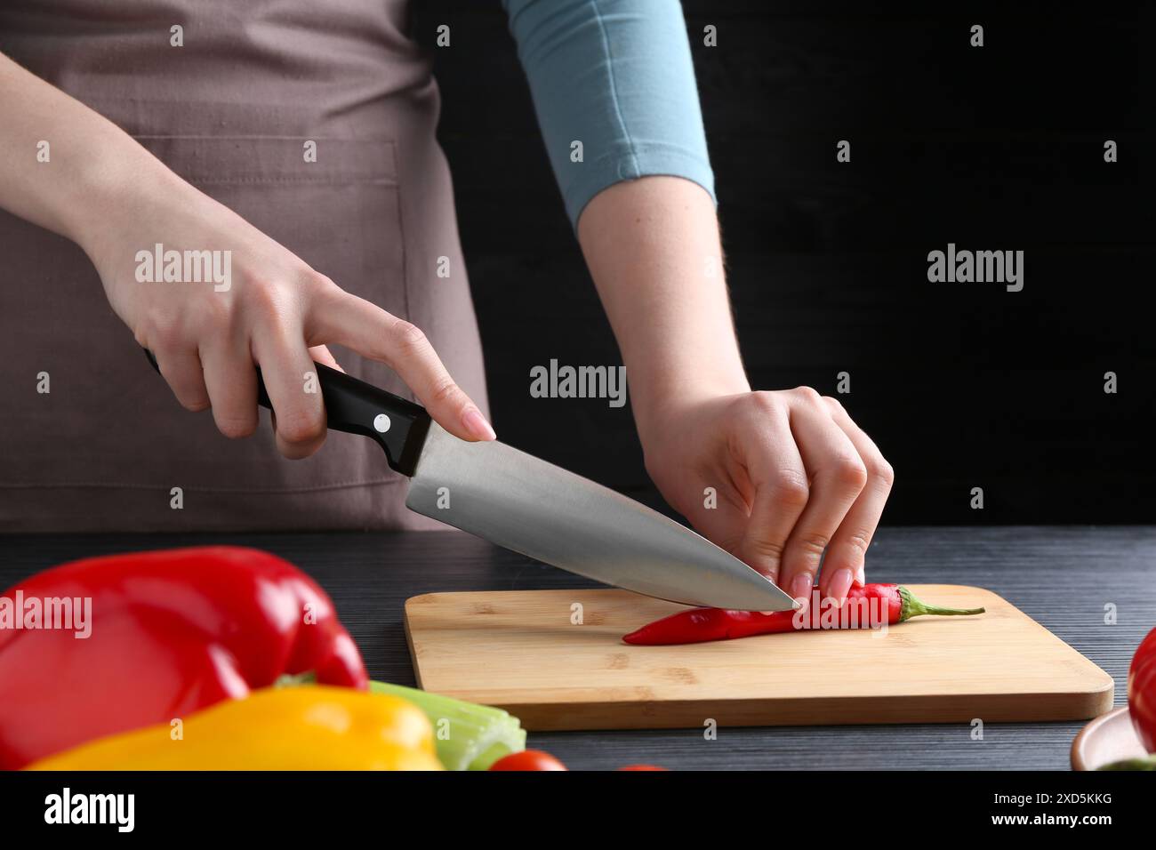 Healthy food. Woman cutting chili pepper at black wooden table, closeup ...