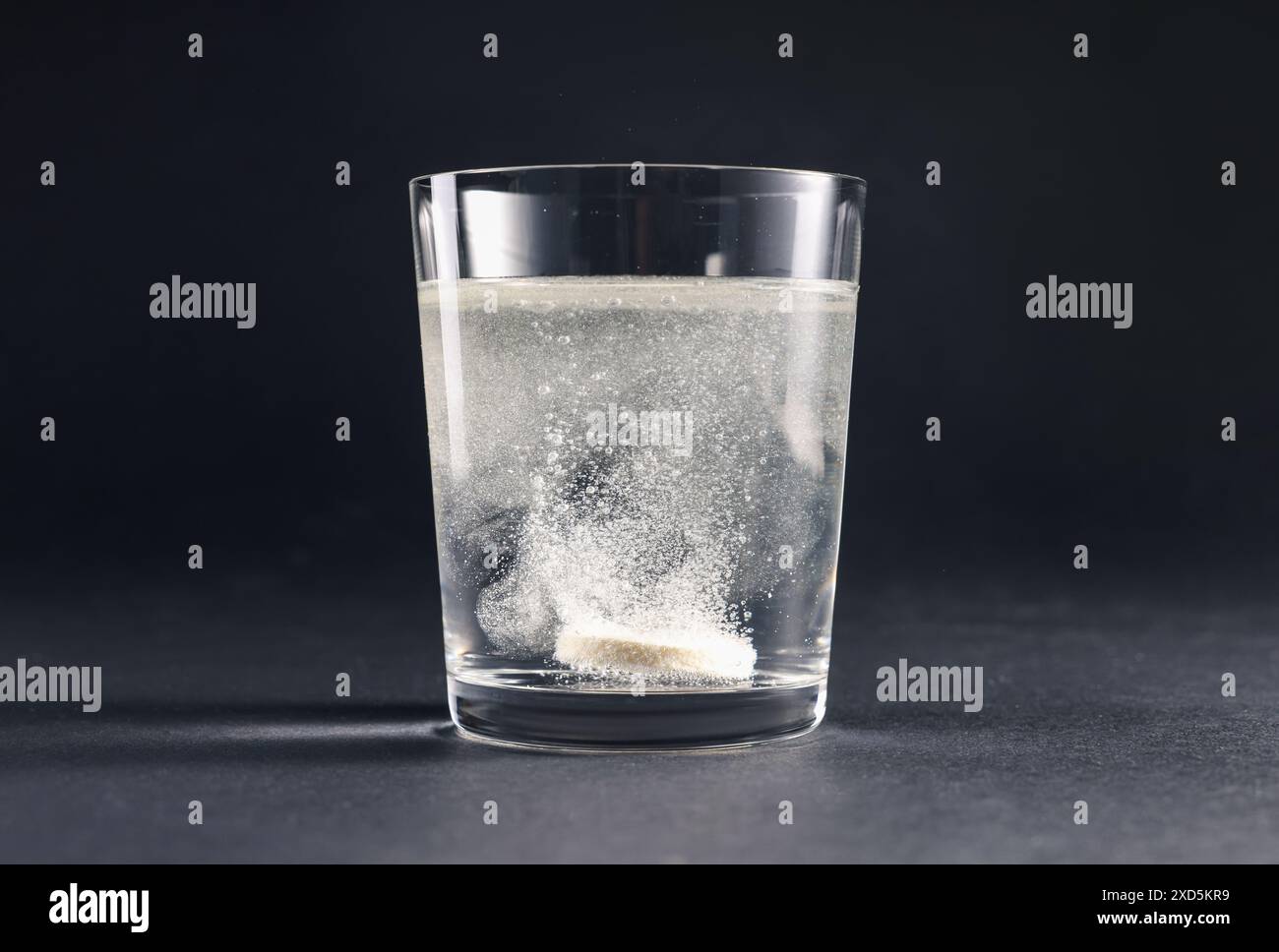 Effervescent pill dissolving in glass of water on grey table Stock ...
