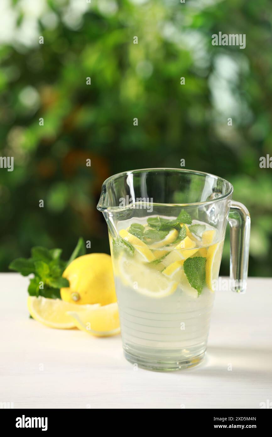 Refreshing lemonade with mint in jug and fruits on light table against ...