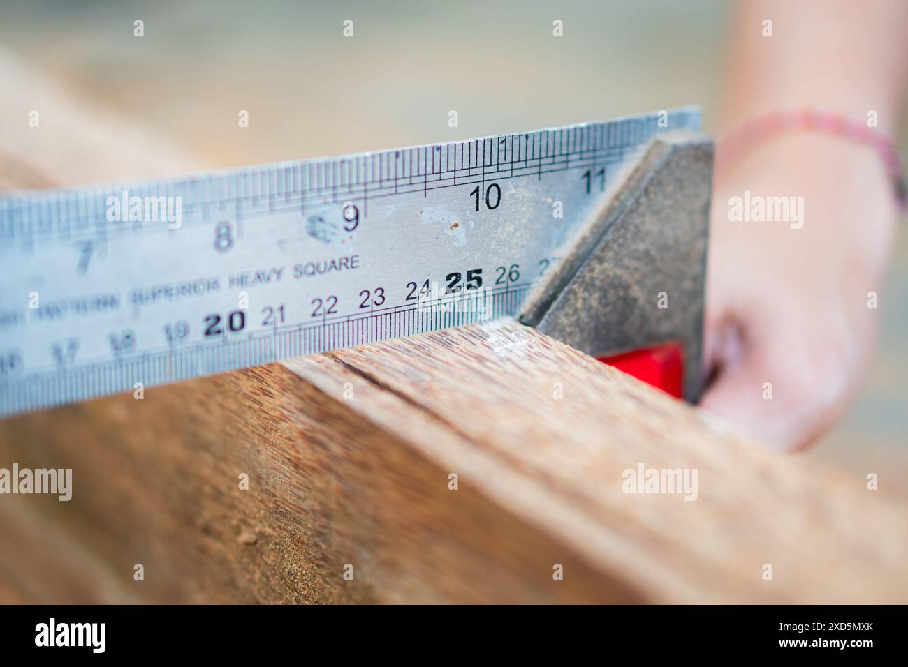 Close-up of a person using a metal square ruler to measure a piece of ...