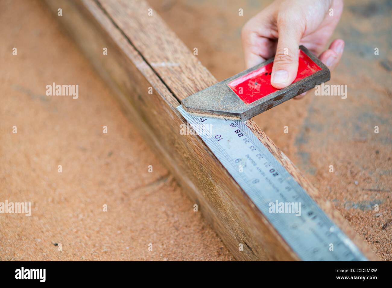 A person using a metal ruler and a red-handled tool to measure and mark ...