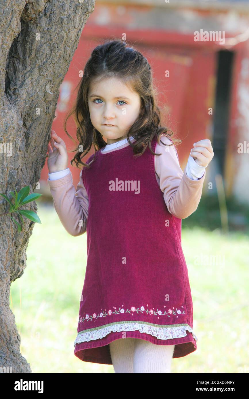 portrait of a serious beautiful little girl next to the tree in the ...