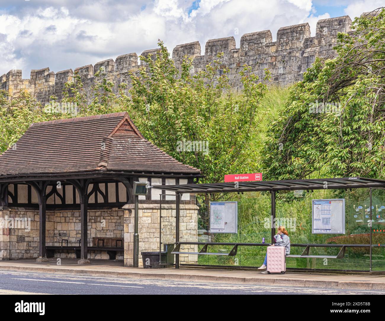 A bus stop underneath historic city walls. A passenger waits, sat with ...