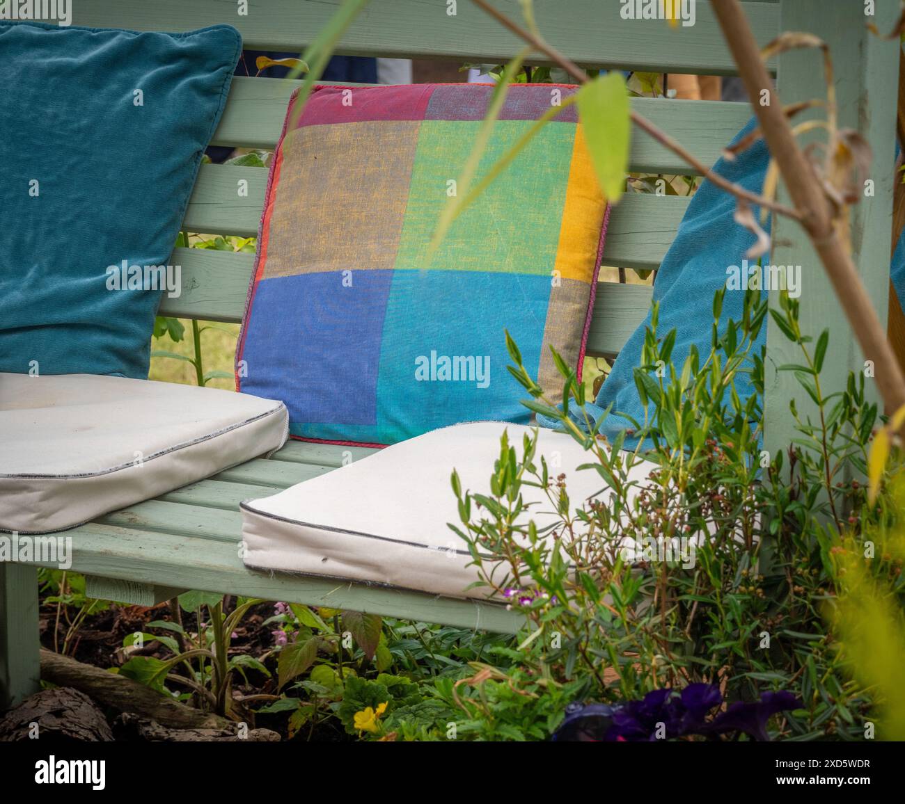 Empty garden bench painted in a soft green and decorated with cushions ...